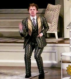A Man In A Suit And Tie Standing Next To A Stair Case With A Chair Behind Him