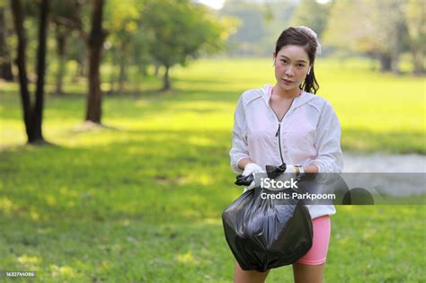 아침 달리기 후 젊은 아름다운 아시아 자원 봉사 여성은 쓰레기 봉투를 들고 공원 잔디밭에서 쓰레기를 줍고 자원 봉사 환경 청소 중에 플라스틱 병과 전체 검은색 가방을 보여