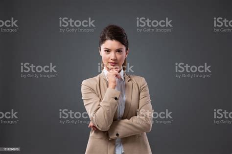 사업에 여자 회색 배경 앞에 서있는 자신감 있는 성인 사업가의 초상화가 그녀의 턱에 손을 얹고 있었다 흰색 셔츠와 베이지 색