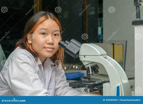 Cute Scientist Schoolgirl In Lab Coat Looks Through Microscope For