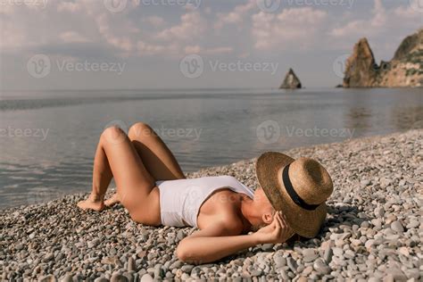 A Woman Is Laying On The Beach Wearing A Straw Hat She Is Wearing A