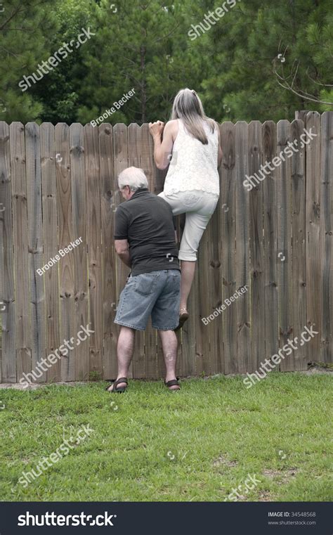Her Husband Helps Her Peek Over The Fence To See What The Neighbors Are