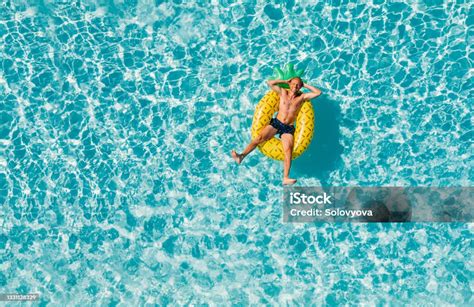 거대한 팽창식 옐로우 파인애플 튜브에 푸른 수영장 파도에 떠있는 선글라스 선글라스를 입은 쾌활한 중년 남성이 웃고 있습니다 고급 리조트 컨셉으로 여름 휴가를 식히세요 튜브