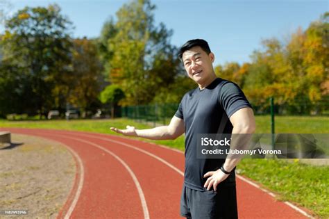 젊은 아시아 운동선수 코치가 경기장에 서서 육상 트랙을 손으로 가리키고 있다 스포츠를 훈련 발표 및 대중화에 초대합니다 교사