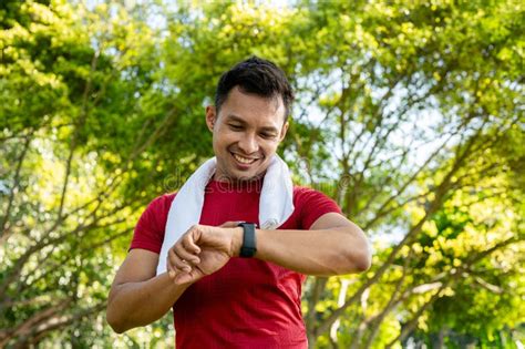 A Happy Asian Man In Sportswear Checks His Calorie Count On His Smartwatch While Jogging In A