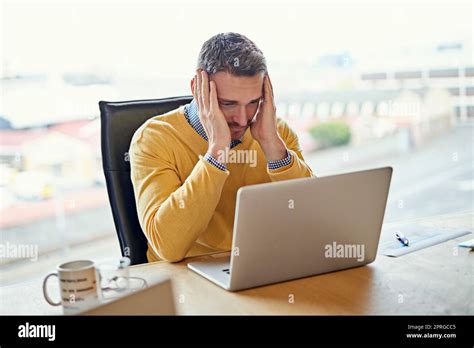 Stressful Day At The Office Shot Of A Businessman Working On His Laptop At His Desk Stock Photo