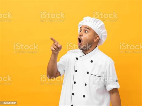 웃는 젊은 잘 생긴 아시아 남자 요리사가 유니폼을 입고 노란색 배경 빈 공간에 손가락을 대고 서있는 모자를 쓰고 텍스트 요리 남자 직업 요리사 또는 빵집 부엌 레스토랑과