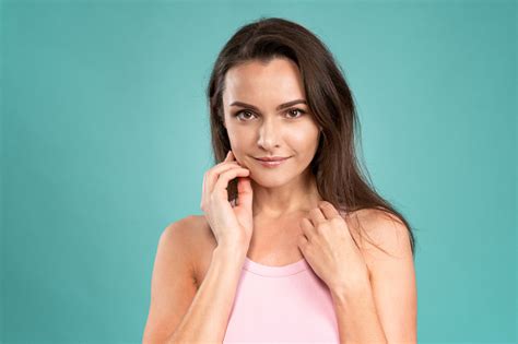 그녀의 목과 병아리에 손으로 서 그녀의 얼굴을 보습 하는 메이크업 아름 다운 여자 파란색 배경에 부드럽게 매력적인 갈색 머리