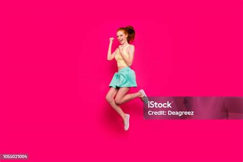 매력적인 긍정적인 장난 다행 빨간 머리 여자 Tanktop와 포니 테일 승리 몸짓 짧은 스커트에 공기 점프의 전체 몸 길이 크기 밝고 선명한 적자 색 배경 위에 절연 날기에