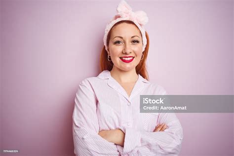 분홍색 고립 된 배경 행복 한 얼굴 카메라를 보고 교차 된 팔 미소 에 서 잠옷을 입고 젊은 아름 다운 빨간 머리 여자 긍정적