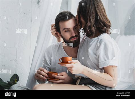 Beautiful Young Couple Kissing While Having Coffee At Home In Morning