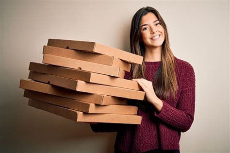 행복한 얼굴 서서 치아를 보여주는 자신감 미소와 함께 미소와 흰색 배경 위에 서 배달 이탈리아어 피자 상자를 들고 젊은 아름다운