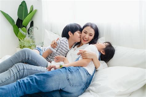 아늑한 집에서 사랑스러운 행복한 아시아 가족 아들과 딸은 침실에서 함께 휴식을 취하고 장난치는 엄마와 키스합니다 부모와 자녀의