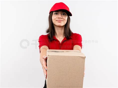 身穿红色制服、头戴帽子的年轻送货女孩伸出盒子包裹，微笑着友好地站在白墙上产品实拍免费下载格式626像素编号53613190 千图网