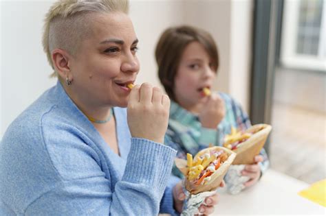 짧은 머리를 가진 백인 여자는 아들과 함께 감자 튀김과 자이로를 먹고 있습니다 쾌활한 여성과 패스트푸드점에서 식사를 즐기는