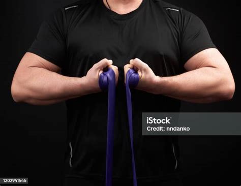 검은 옷을 입고 근육질의 몸을 가진 운동 선수는 파란색 고무로 신체 운동을하고 있습니다 건강한 생활방식에 대한 스톡 사진 및