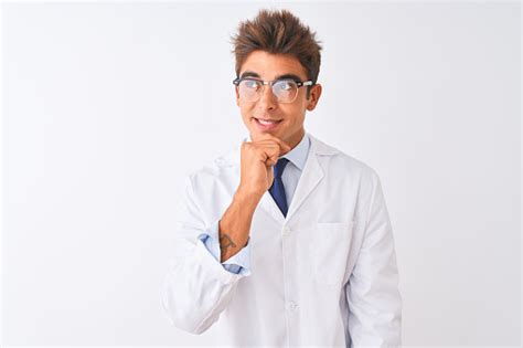 젊은 잘생긴 Sciencist 남자 안경과 코트 위에 고립 된 흰색 배경 에 턱에 대 한 생각 Pensive 표현 미소와 사려 깊은 얼굴 의심 개념 과학자에 대한 스톡 사진