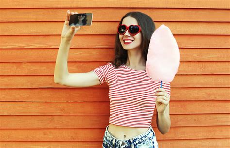 목조 벽 배경에 놀이 공원에서 스마트 폰으로 셀카 사진을 찍는 솜 사탕과 행복한 미소 젊은 여성의 초상화 20 29세에 대한 스톡 사진 및 기타 이미지 Istock