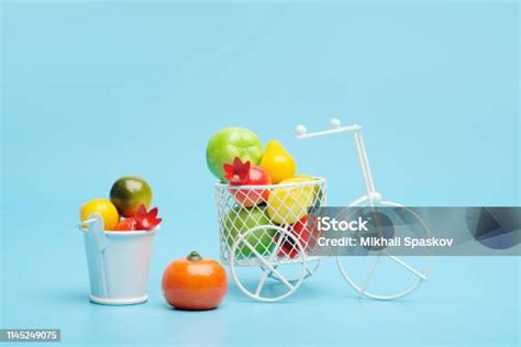 미니 과일로 채워진 바구니가 있는 화이트 와이어 자전거 야채와 과일 양동이 근처 파란색 배경입니다 과일과 채소를 수확 하 고