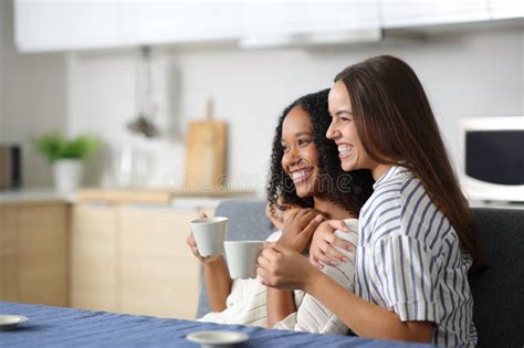 Happy Interracial Lesbian Couple Hugging In The Kitchen Looking Away