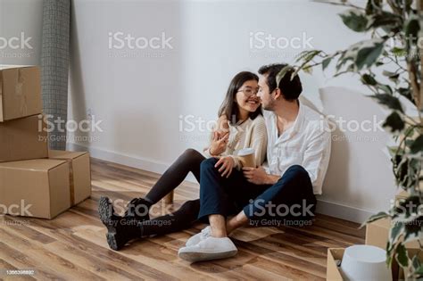사랑에 빠진 부부는 새 아파트의 벽에 앉아 있고 흰 셔츠를 입은 용감한 남자가 웃는 예쁜 여자를 껴안고 커피를 마시고 유혹하고