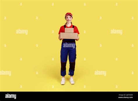 Full Length Portrait Of Courier Woman Standing With Two Parcels In