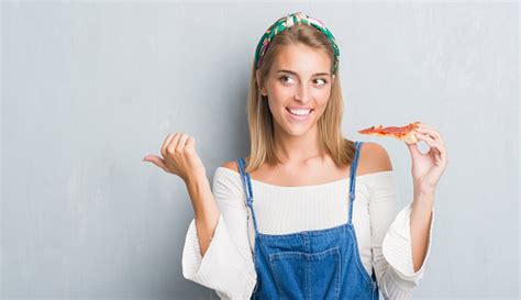 먹는 페퍼로니 피자 조각 고 행복 얼굴 미소와 측면까지 손가락으로 보여주는 그런 지 회색 벽에 아름 다운 젊은 여자 가리키기에 대한 스톡 사진 및 기타 이미지 Istock