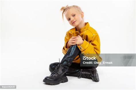 가죽 겨자 재킷 검은 뱀 질감 레깅스와 부츠로 스튜디오 바닥에 앉아있는 예쁜 금발 어린 소녀 하이 패션 전체 길이 서있는 자세