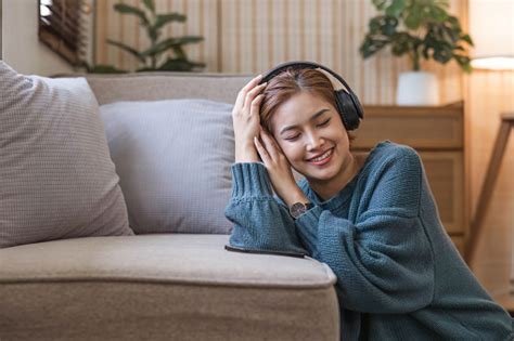 집에서 소파 근처에 앉아 휴대폰으로 음악을 듣는 행복한 아시아 여성 아침에 헤드폰을 끼고 휴식을 취하는 웃는 소녀 휴식을 취할