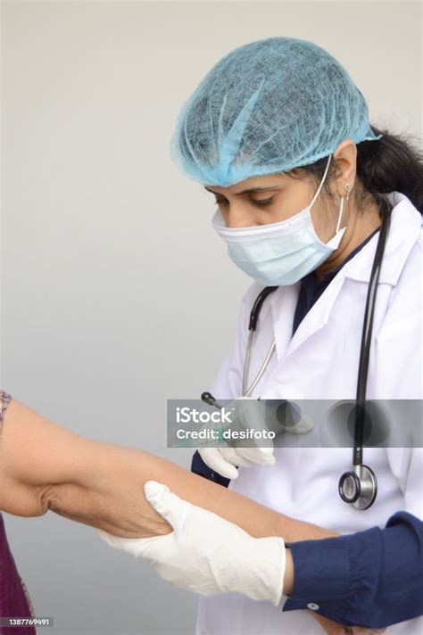 외과 마스크 모자 흰색 실험실 코트를 입은 여성 또는 여성 의사 목에 청진기가 주사기 바늘 주사를 손에 들고 환자에게 복용량을 투여하고 텍스트를 위한 복사 공간이있는 회색