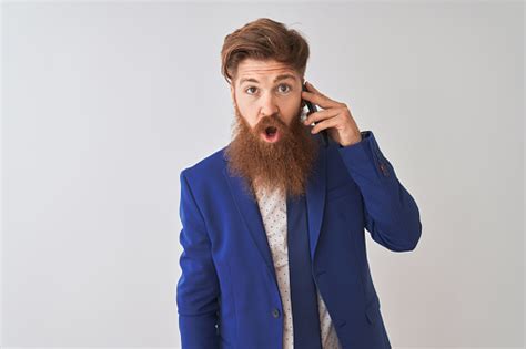 젊은 빨간 머리 아일랜드어 사업가는 깜짝 얼굴 두려움과 두려움 표정으로 흥분 충격에 무서워 고립 된 흰색 배경을 통해 스마트