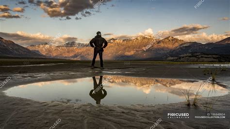 Man Standing With Reflection In A Pool Of Water Looking Out Over The