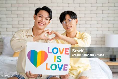 게이 또는 Lgbt 남자 커플은 침대에 앉아서 자신의 감정을 표현하고 그들의 관계를 자랑스럽게 여기는 배너를 들고 있습니다 2