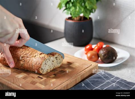 Woman Cutting Loaf Of Whole Grain Bread With Large Knife On Cutting