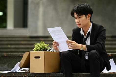 해고에 대한 나쁜 소식을 읽고 개인 물건 상자를 들고 건물 계단에 앉아 있는 좌절한 슬픈 사업가 25 29세에 대한 스톡 사진