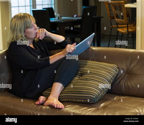 Femme Blonde Est Assise Sur Son Canapé En Cuir Avec Une Tablette Et