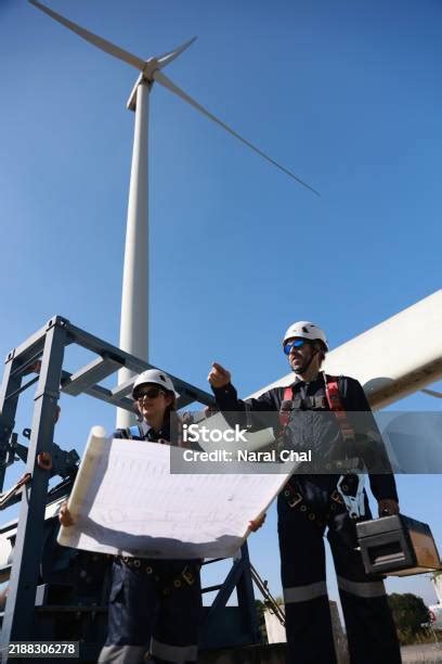 두 명의 남성과 여성 풍력 터빈 엔지니어가 화창한 날 대형 풍력 터빈의 바닥에서 작동하는 청사진과 함께 풍력 터빈의 블레이드를 검사합니다 2명에 대한 스톡 사진 및 기타