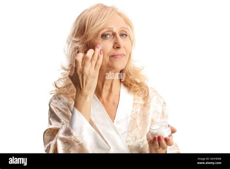 Belle femme mûre dans un peignoir appliquant la crème faciale anti âge