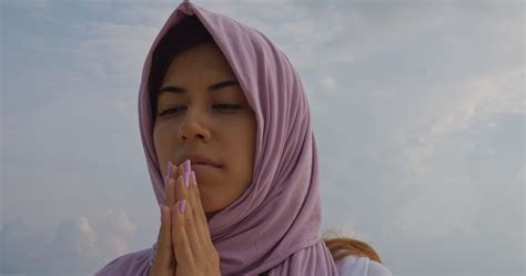 분홍색 히잡을 쓴 젊은 이슬람 여성이 눈을 감고 밖에서 기도하고 있다 분홍색 손톱을 가진 무슬림 여성은 구름 라마단 영혼의 정화를 배경으로 기도하기 위해 손바닥을 접었다