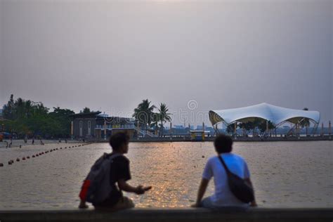 Two Men Sit Back To Back Looking At The Sea At Ancol Beach In The