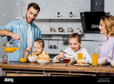 handsome father pouring orange juice in glass while children eating ...