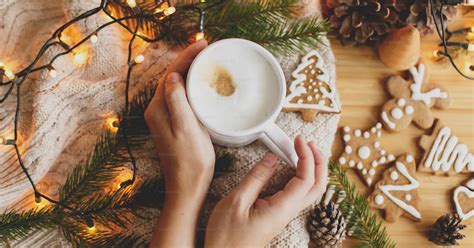 크리스마스 진저 브레드 쿠키 아늑한 니트 스웨터 소나무 콘과 조명이있는 전나무 가지를 배경으로 따뜻한 커피를 들고 있습니다