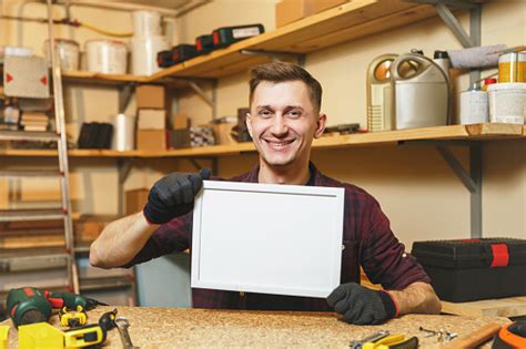 격자 무늬 셔츠에 잘생긴 백인 젊은 남자 장갑 나무 테이블에서 목공 워크숍에서 빈 프레임 다른 도구와 장소 텍스트에 대 한 빈 자리와 광고에 대 한 공간을 복사 합니다