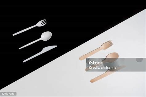 대각선으로 분할 된 흑백 배경에 나무 칼 옆에 일회용 플라스틱 숟가락 포크와 칼 생태학적 대 비생태학적 0명에 대한 스톡 사진