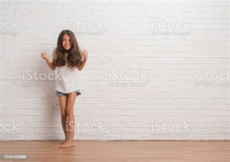 흰색 벽돌 벽 축 하에 젊은 히스패닉 아이 Stading 놀라게 무기 제기와 성공을 위한 깜짝 놀라게 고 눈을 엽니다 우승자
