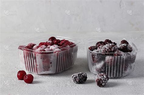 灰色背景上是两个装有冷冻黑莓和樱桃的容器为冬天采集浆果