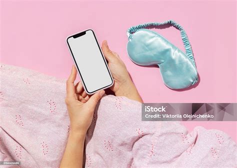 수면 리듬을 확인하기 위해 스마트폰을 들고 있는 여성 아늑한 담요 수면 마스크 및 장치의 빈 화면 건강 관리 수면의 개념
