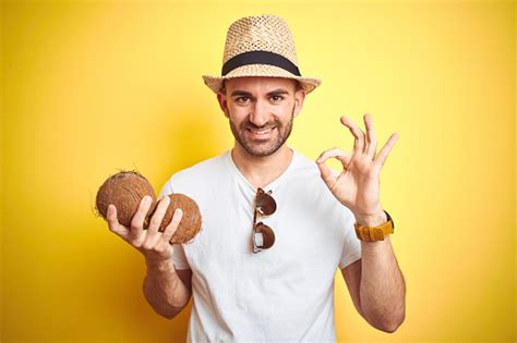 여름 모자를 쓰고 노란 배경 위에 코코넛 과일을 들고 손가락으로 확인 기호를하고 우수한 기호 개념에 대한 스톡 사진 및 기타 이미지 Istock