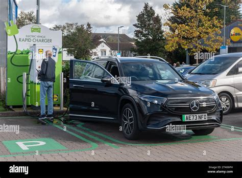 Man Charging His Car Battery At An Electric Vehicle Rapid Charger In A Lidl Supermarket Car Park