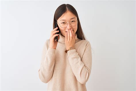 고립 된 흰색 배경 웃음과 손으로 입을 덮는 당황 웃음 험담과 스캔들 개념을 통해 스마트 폰에 이야기 젊은 중국 여성